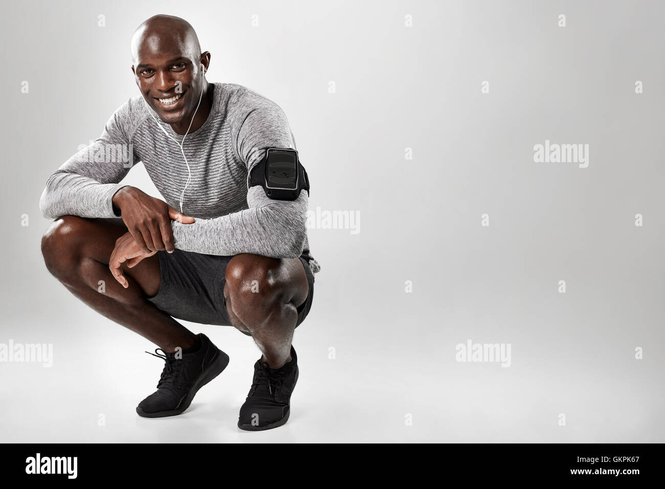 Smiling young african man with mobile phone armband and headphones ...