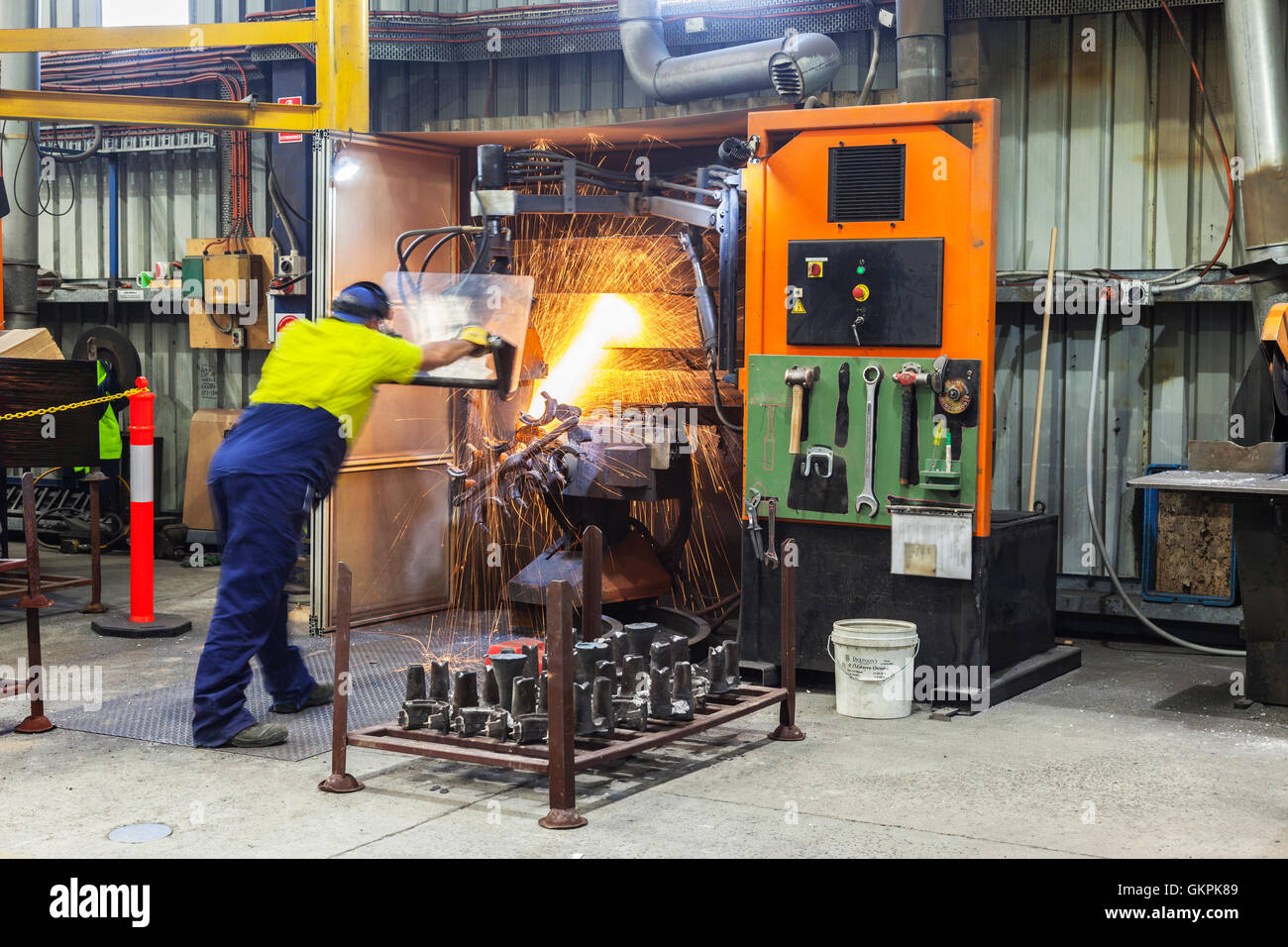 workman grinding and cutting away cast metal components from its ...