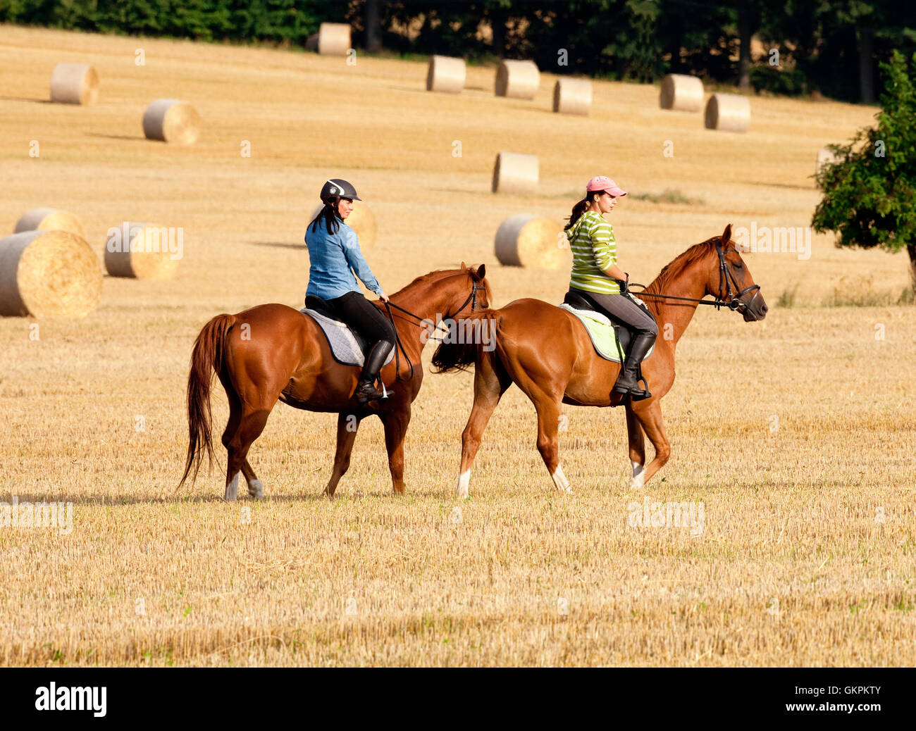 Two Women Horseback Riding in a Field with Bales of Hay Stock Photo - Alamy