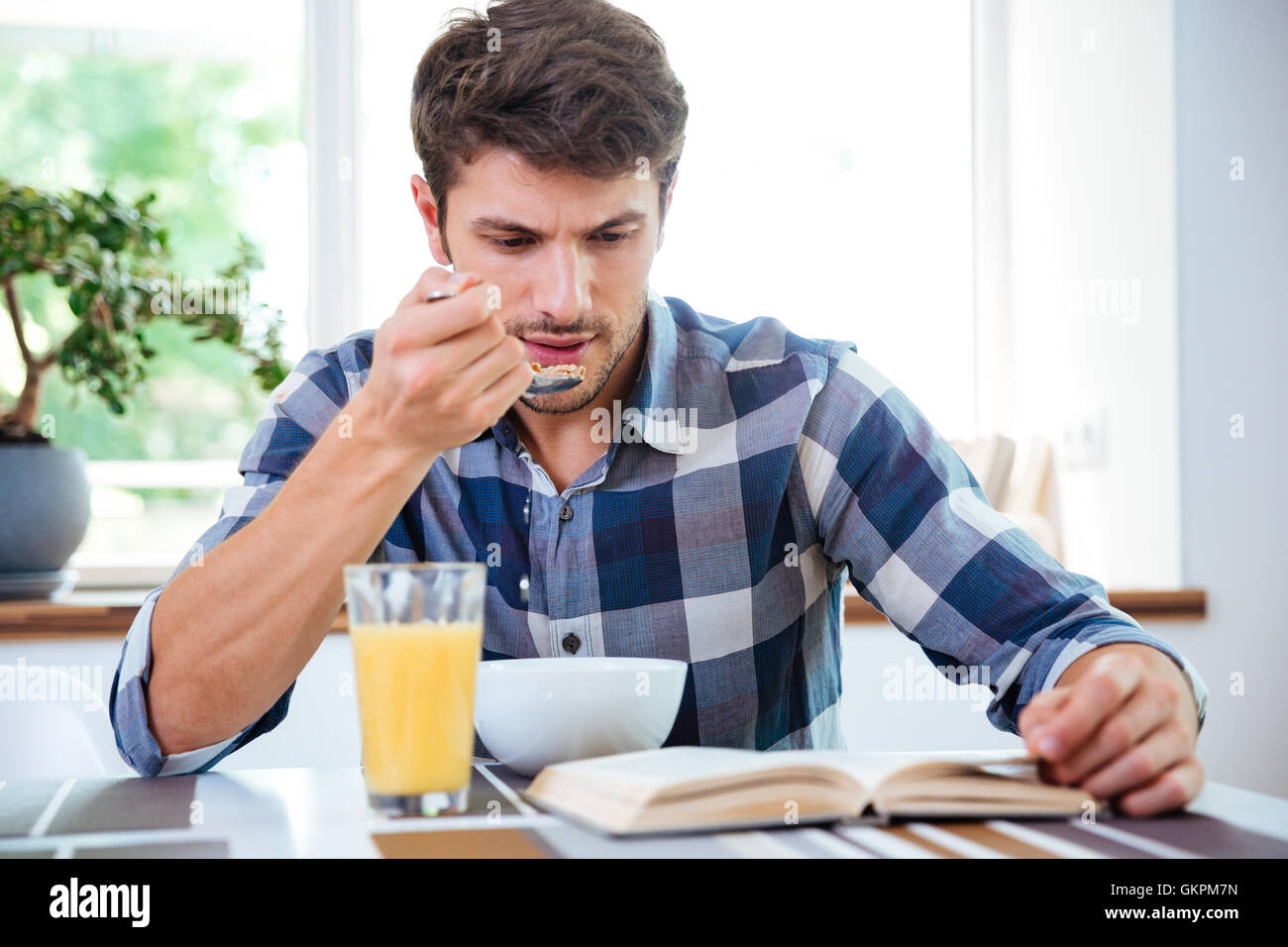 Concentrated young man in plaid shirt reading a book and having ...
