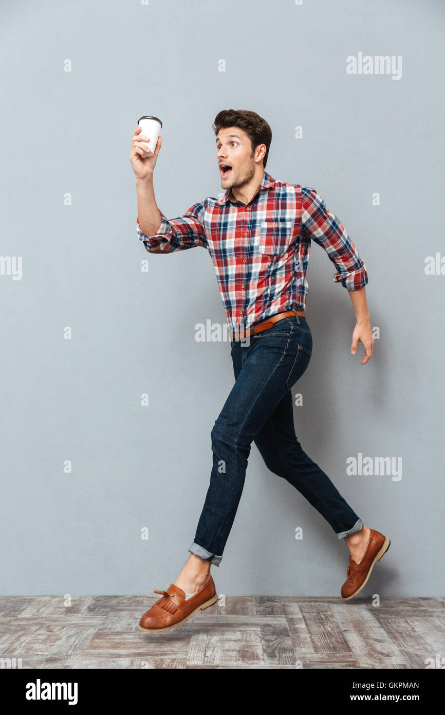 Attractive young man holding cup of takeaway coffee and running over ...