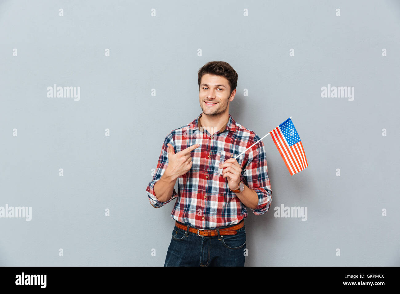 Smiling young man pointing on United States of America flag over grey ...