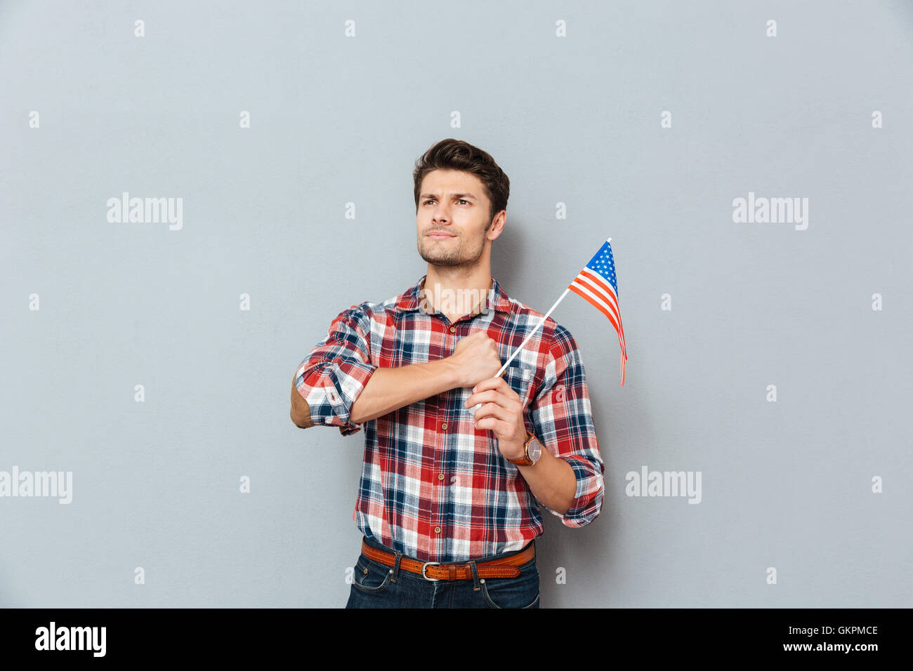 Patriotic proud young man standing and holding flag of USA over grey ...
