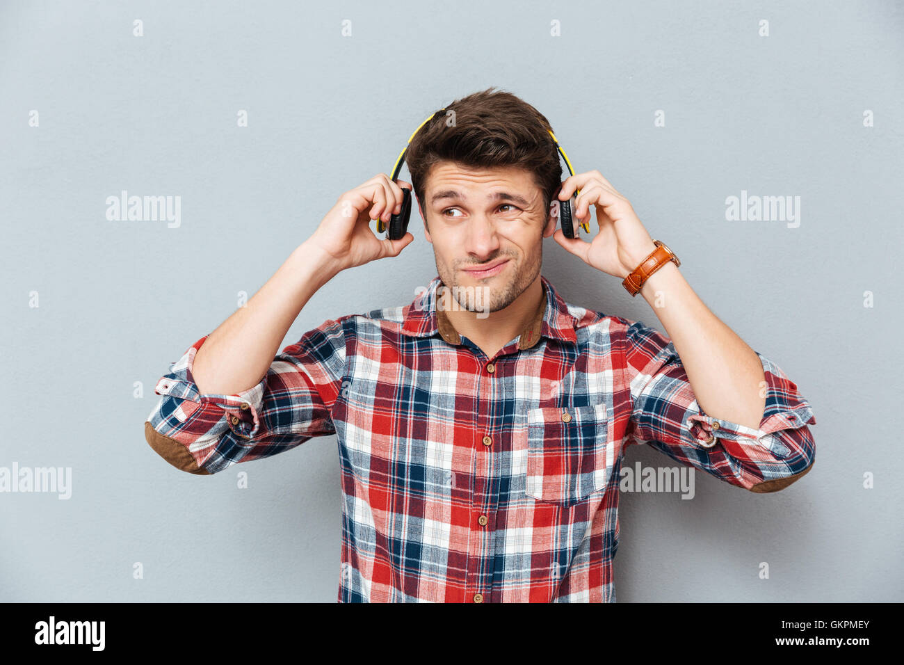 Confused unhappy young man in headphones listening to music over grey ...