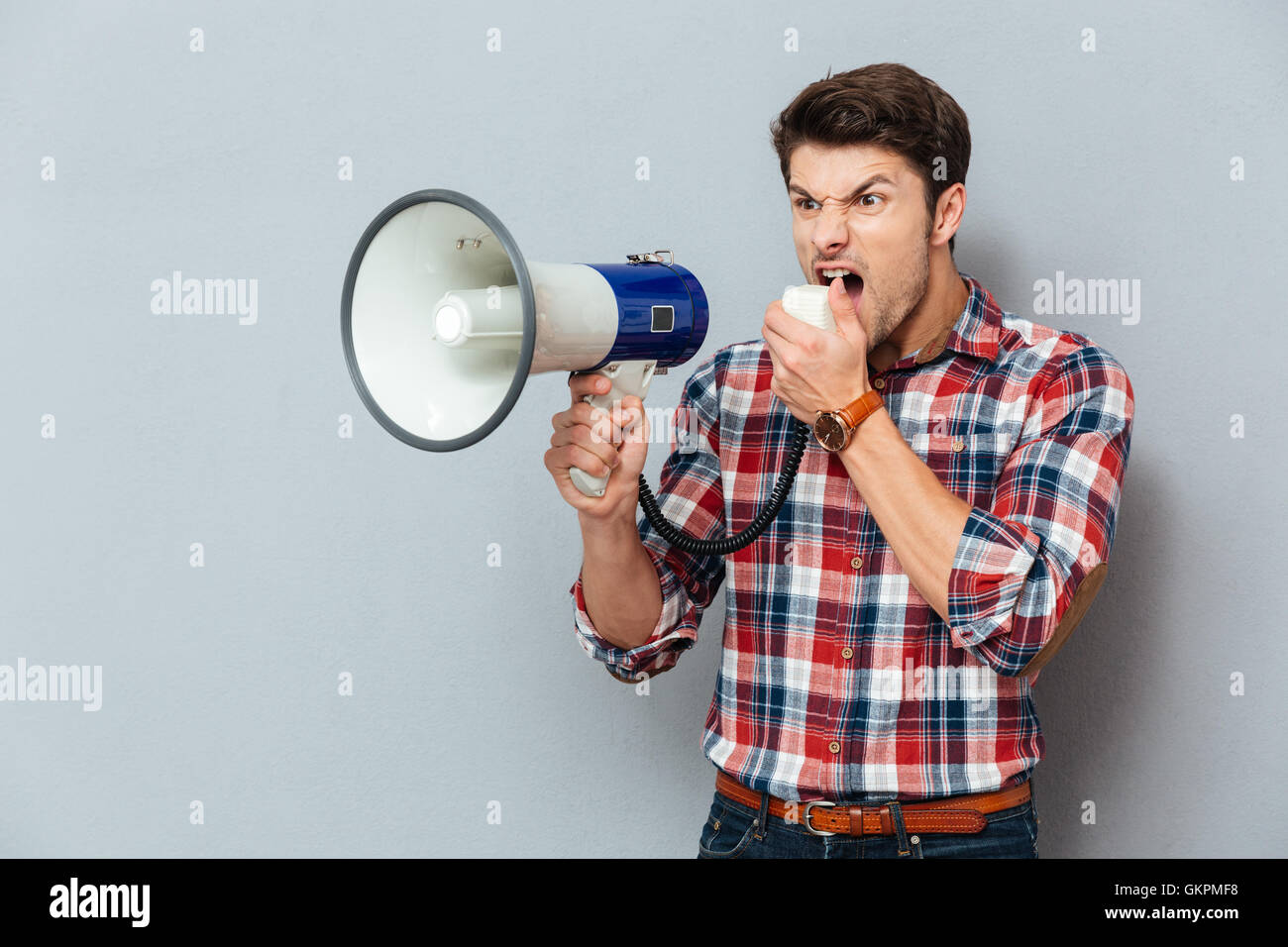 Irritated angry young man in plaid shirt shouting with loudspeaker over ...