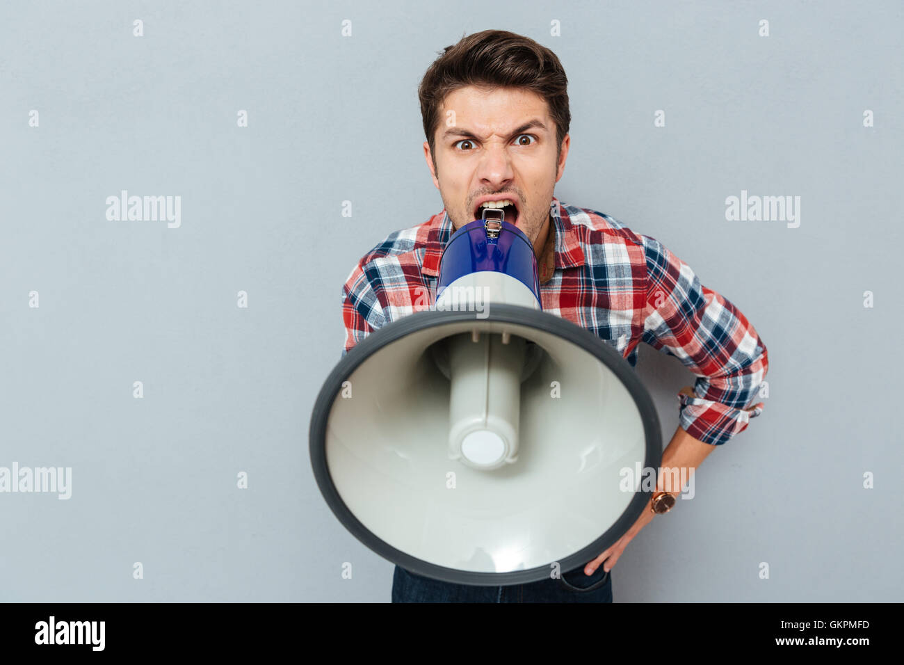 Portrait of a man screaming in megaphone isolated on a gray background ...