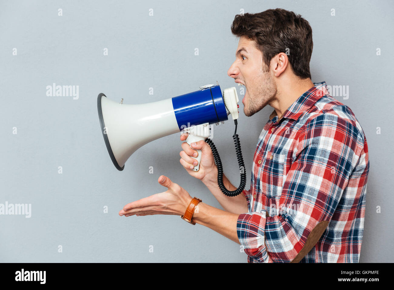 Side view portrait of a casual man yelling into megaphone isolated on a ...