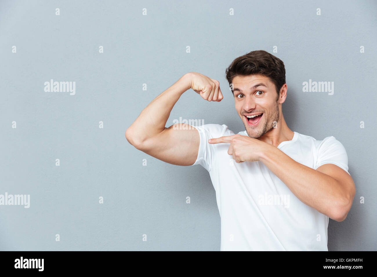 Cheerful casual man pointing finger on his biceps isolated on the gray ...