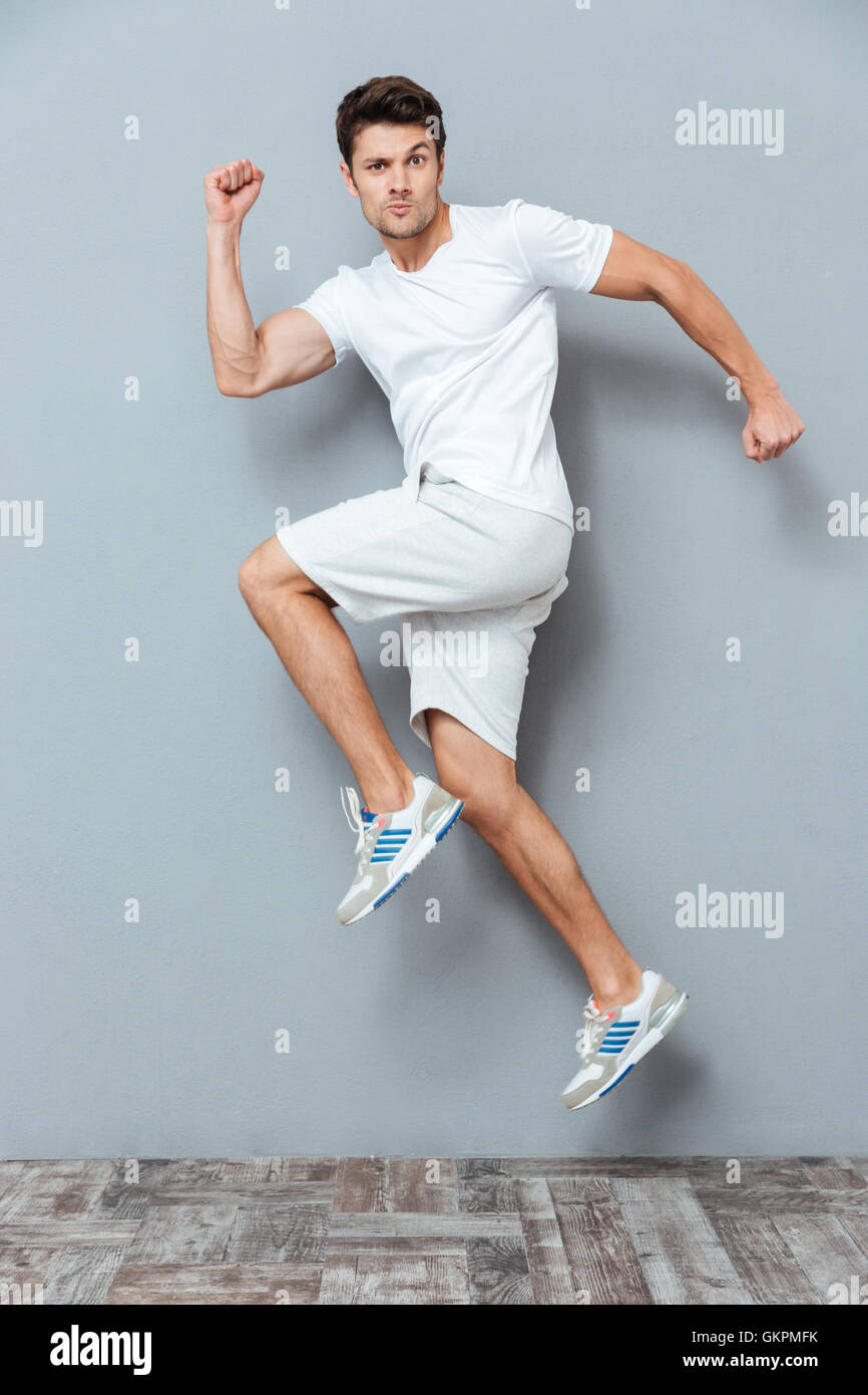 Funny young man jumping over gray background Stock Photo - Alamy