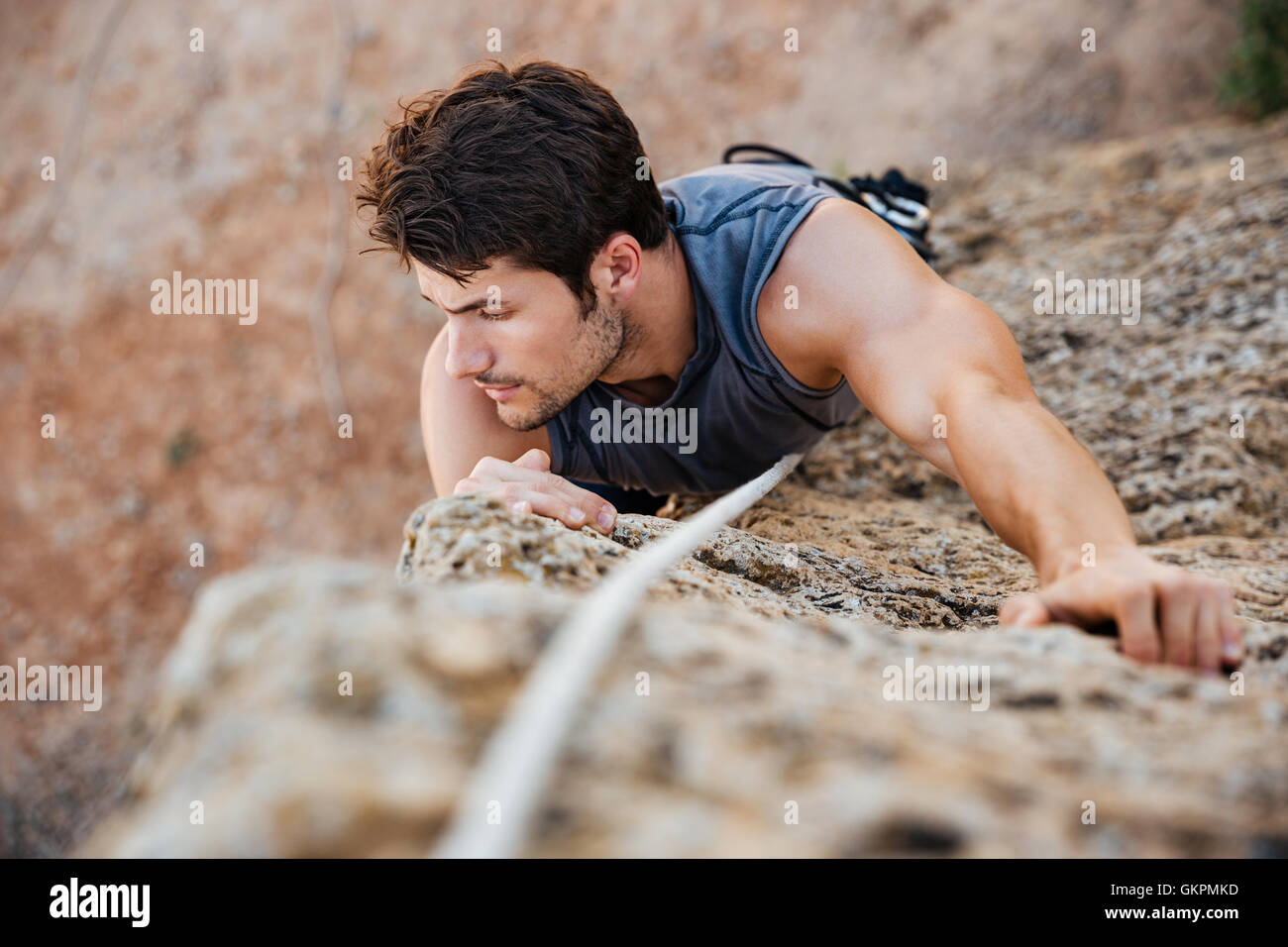 Man reaching for a grip while he rock climbs on a steep cliff Stock ...
