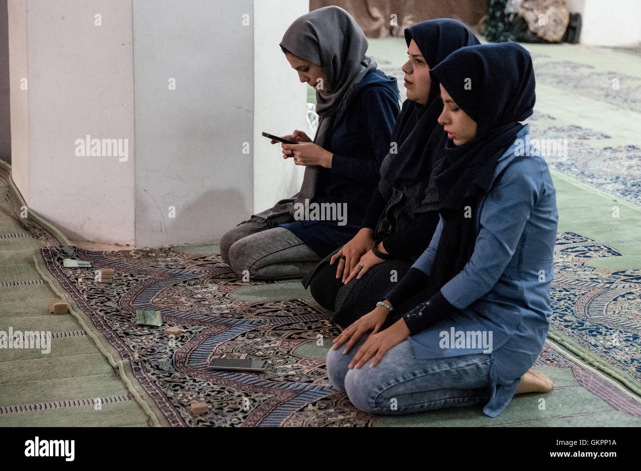 Young Iranian women wearing hijabs kneel to pray with their cell phones ...