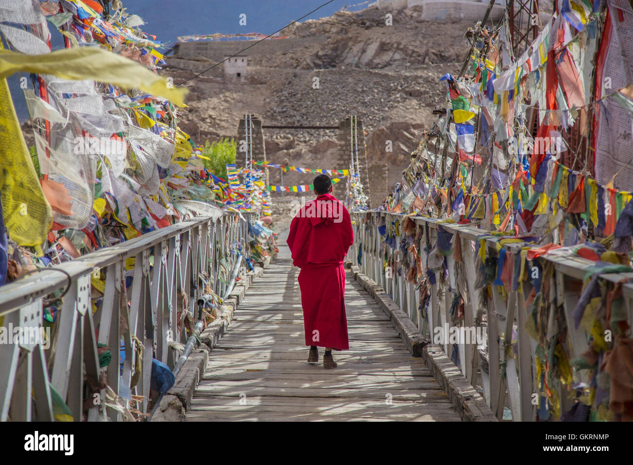 A monk walks on the bridge pathway surrounded by colorful tibetan ...