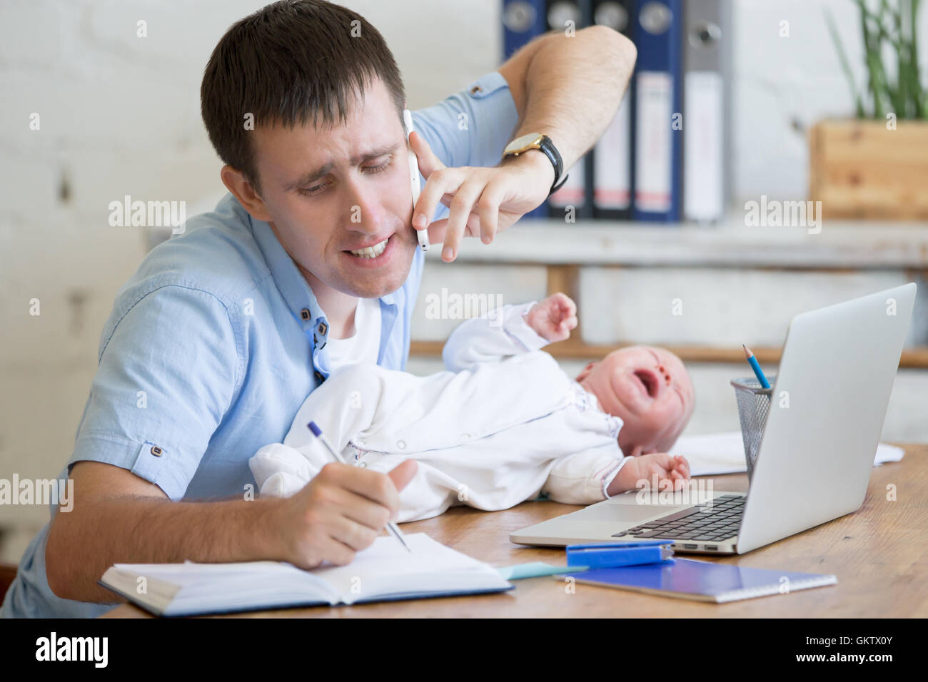 Portrait of young stressed dad trying to work and talk on phone while ...