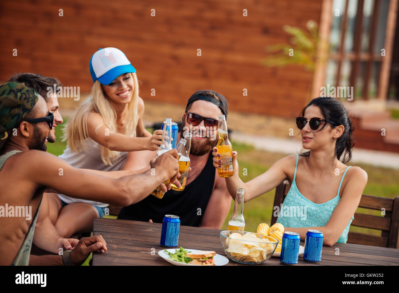 Happy group of teenage friends sitting at table drinking beer and ...