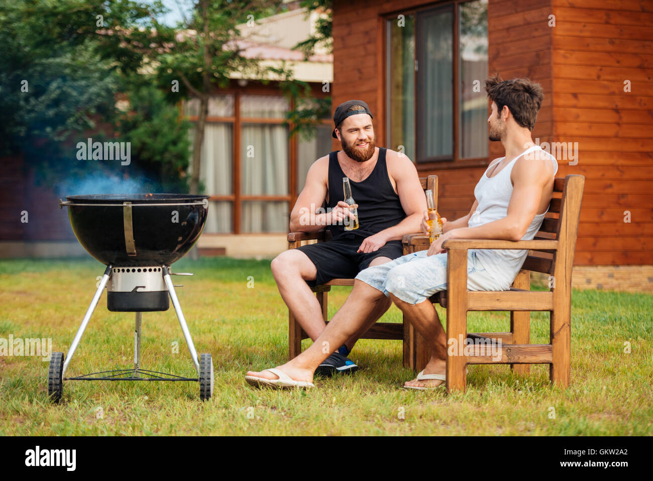 Two young men sitting while preparing barbecue grill in park zone Stock ...