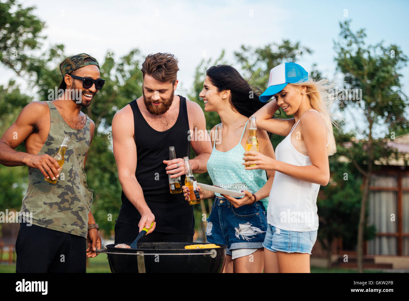 Group of happy young people standing and frying meet on barbeque grill ...