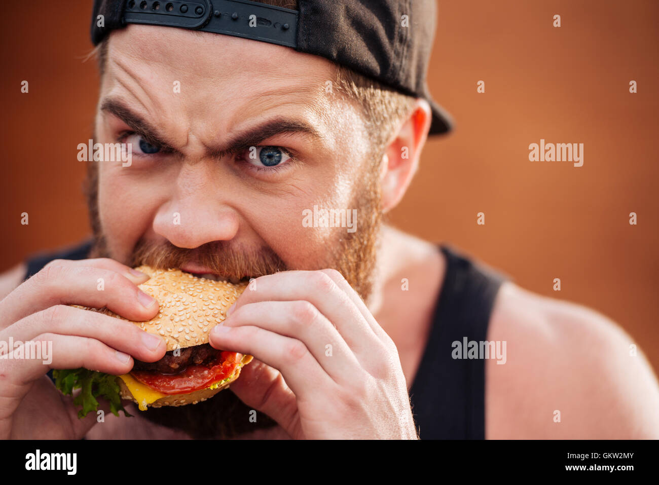 Angry irritated young man in cap eating hamburger outdoors Stock Photo ...