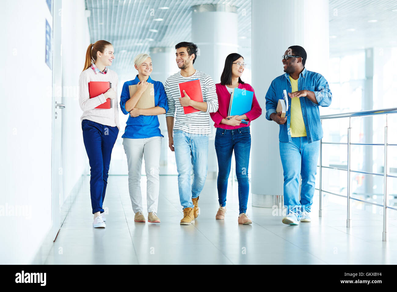 Group of intercultural students walking down corridor after classes ...