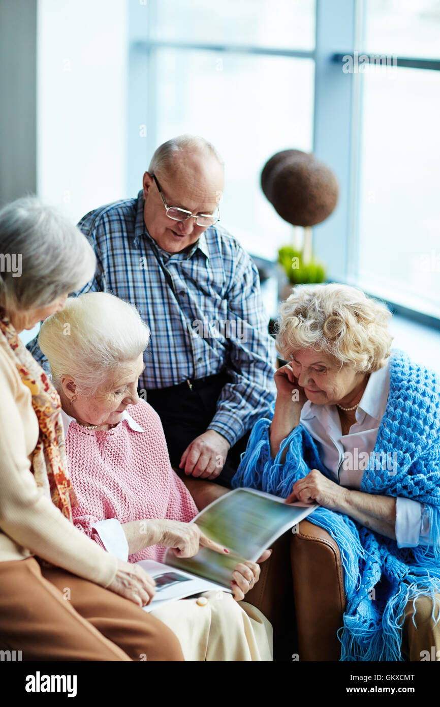 Group of friendly seniors looking through magazine or photo album in ...
