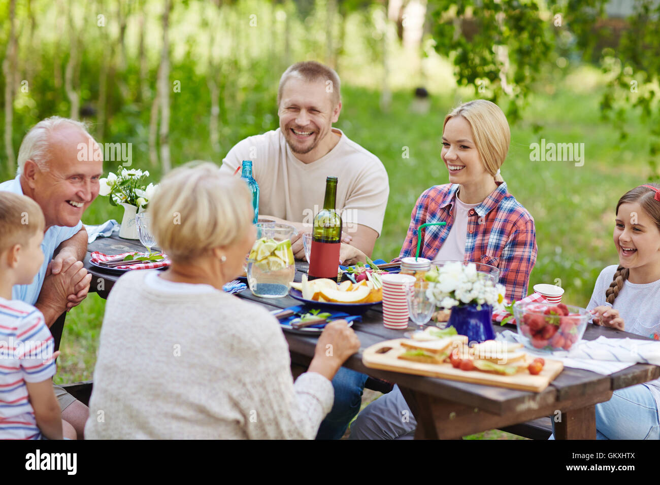 Happy family sitting by dinner table and talking Stock Photo - Alamy