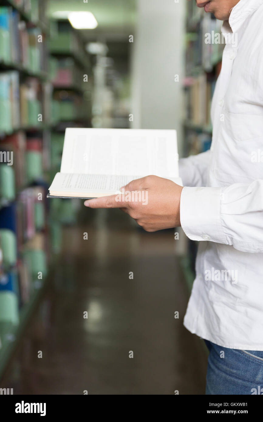 man standing and reading book on floor in aisle in library Stock Photo ...