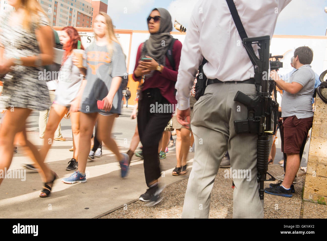 UT students walk past an open carry advocate with a rifle during a ...