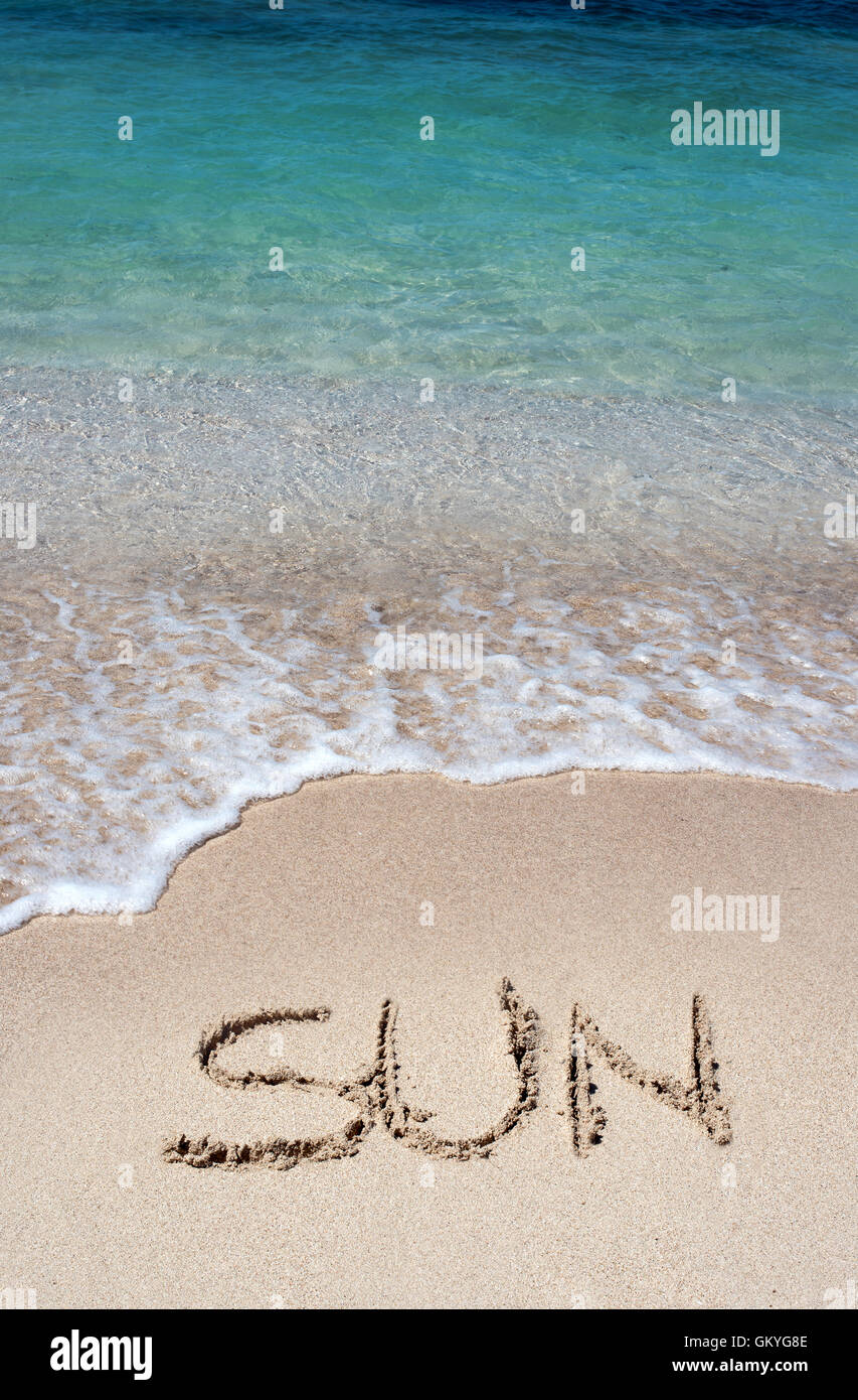The word Sun written in golden beach sand at the edge of gently lapping ...