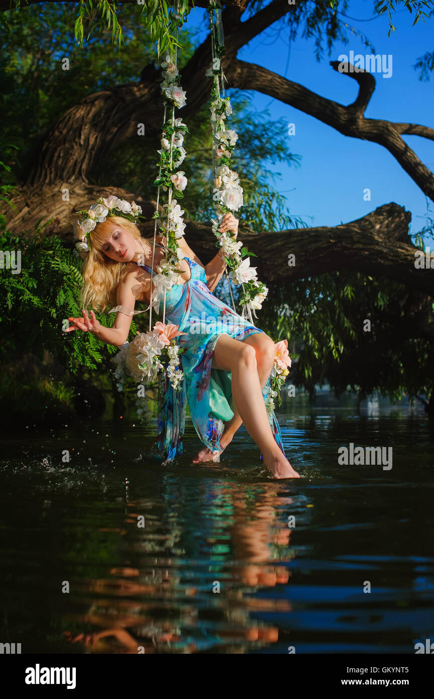 Girl on home made tree swing over river. Swing decorated with flowers ...