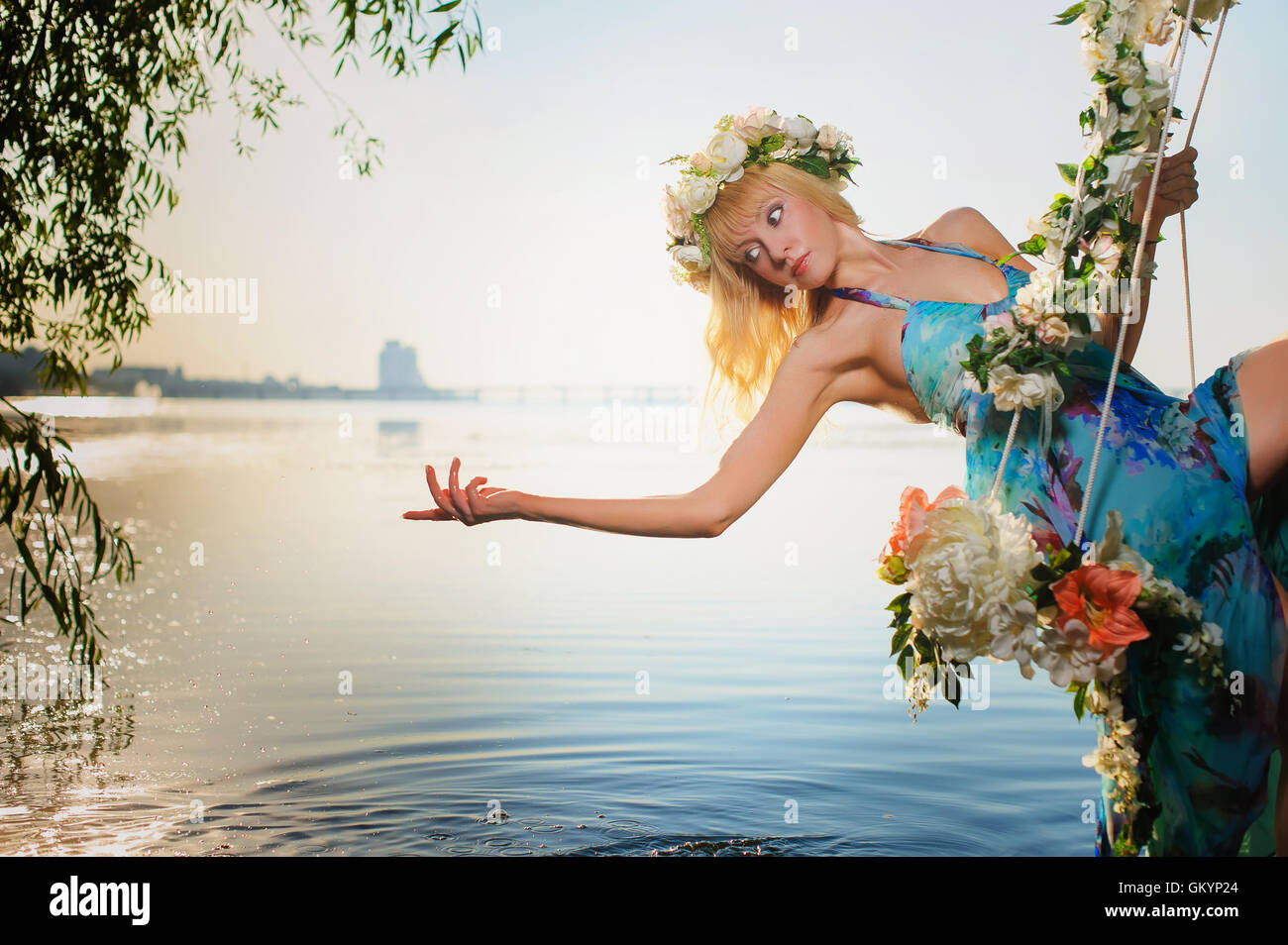 Girl on home made tree swing over river. Swing decorated with flowers ...