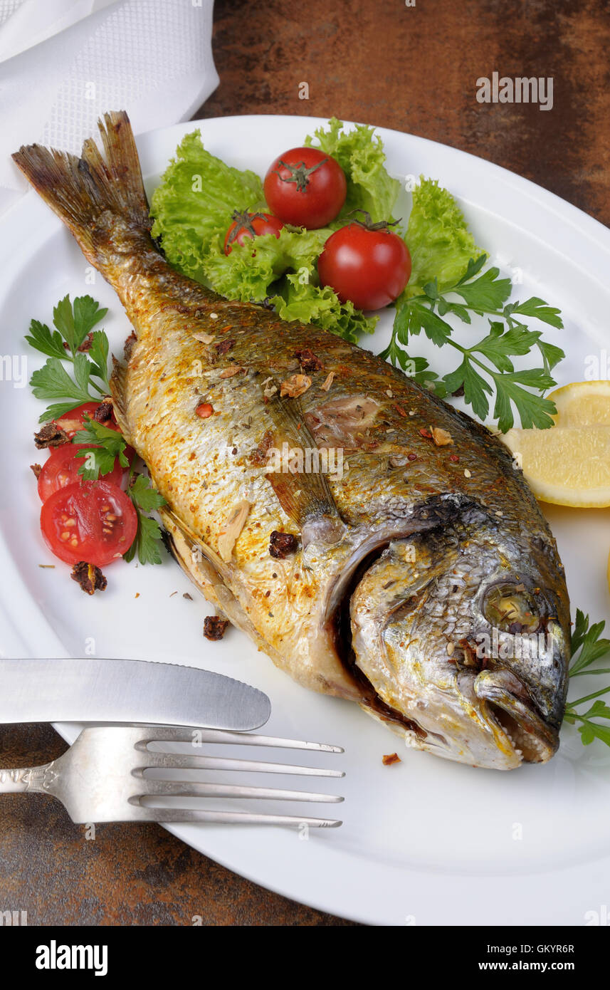 roasted fish Dorado with vegetables garnish and lemon slices on a plate ...