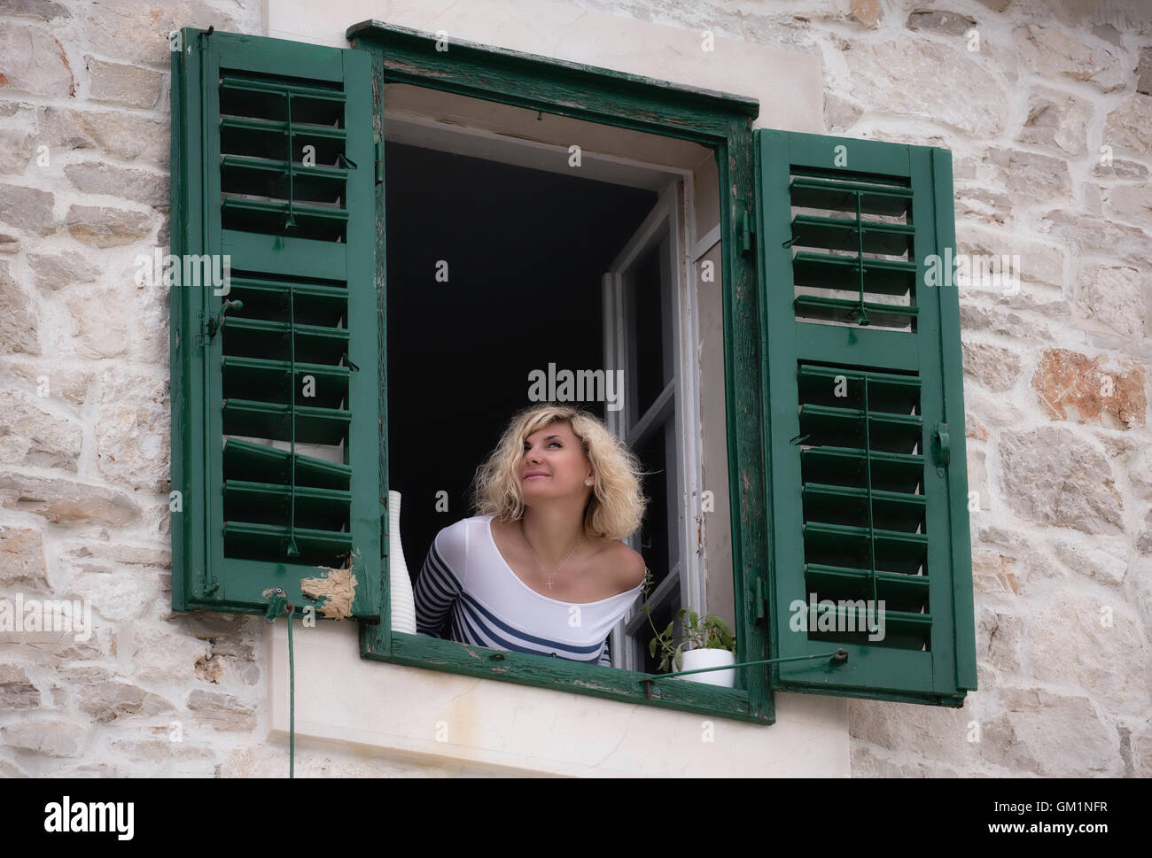 Beautiful blonde woman is looking out the window, leaning on the ...