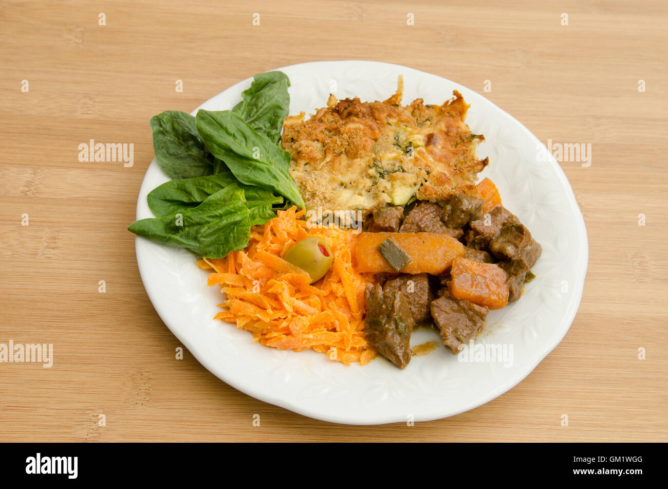 Casserole and pieces of stewed beef on plate with shredded carrots and ...