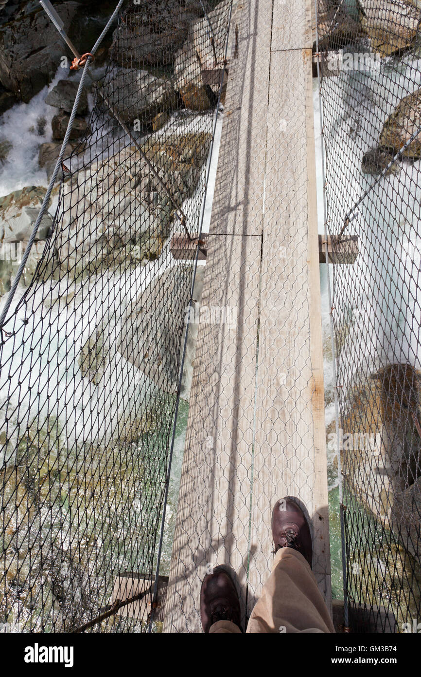 Boots on narrow swing bridge over white water Stock Photo - Alamy