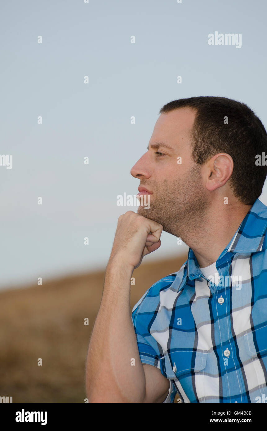 Portrait of a man looking out with his chin resting on his fist wearing ...