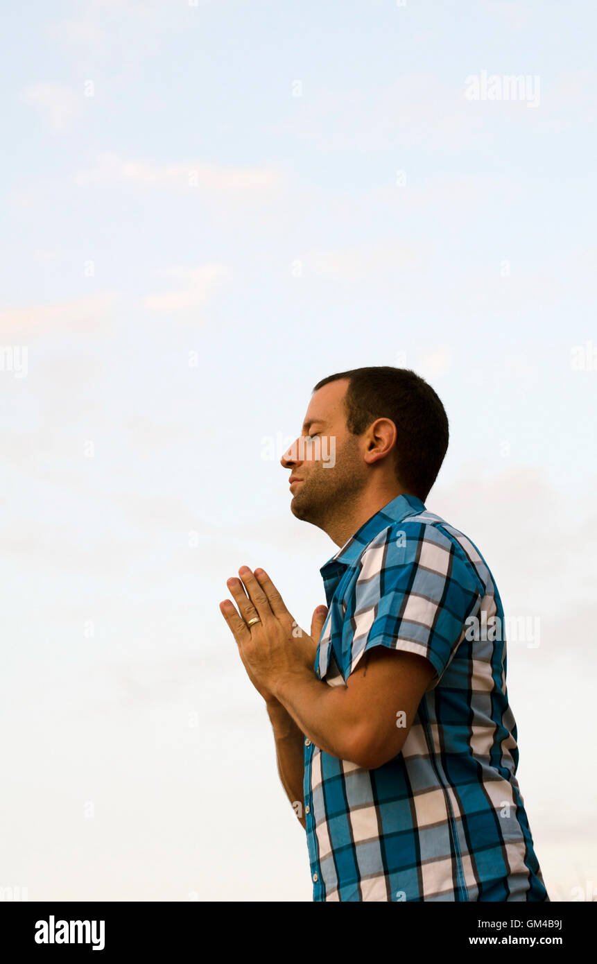 Man standing and praying on a hill outside with his hands clasped ...