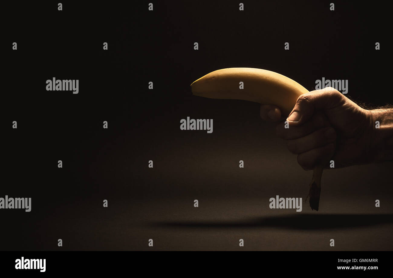 Conceptual composition, male hand holding a banana as gun, symbolically ...