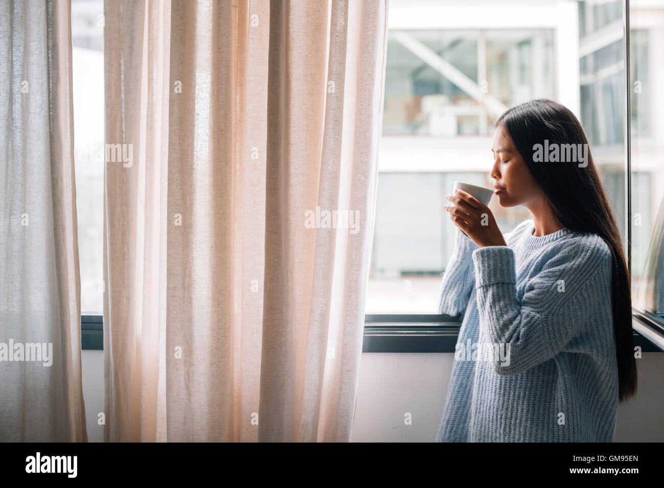 Young woman with cup of coffee standing in front of open window Stock ...