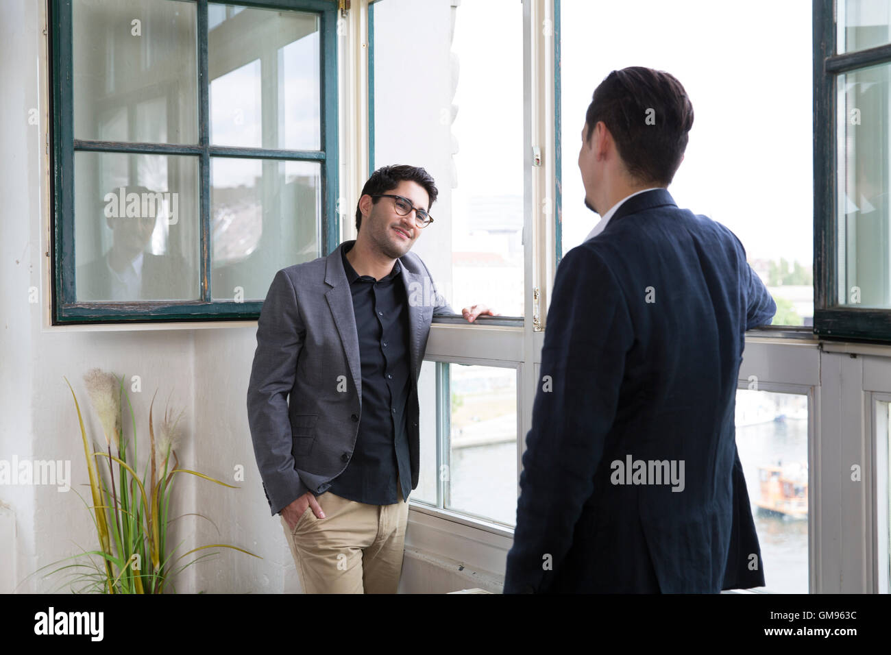 Two businessman standing at the window, talking Stock Photo - Alamy
