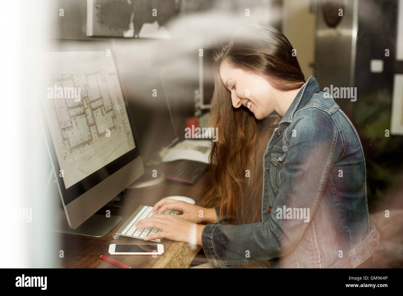 Laughing young woman working on construction plan on computer monitor ...
