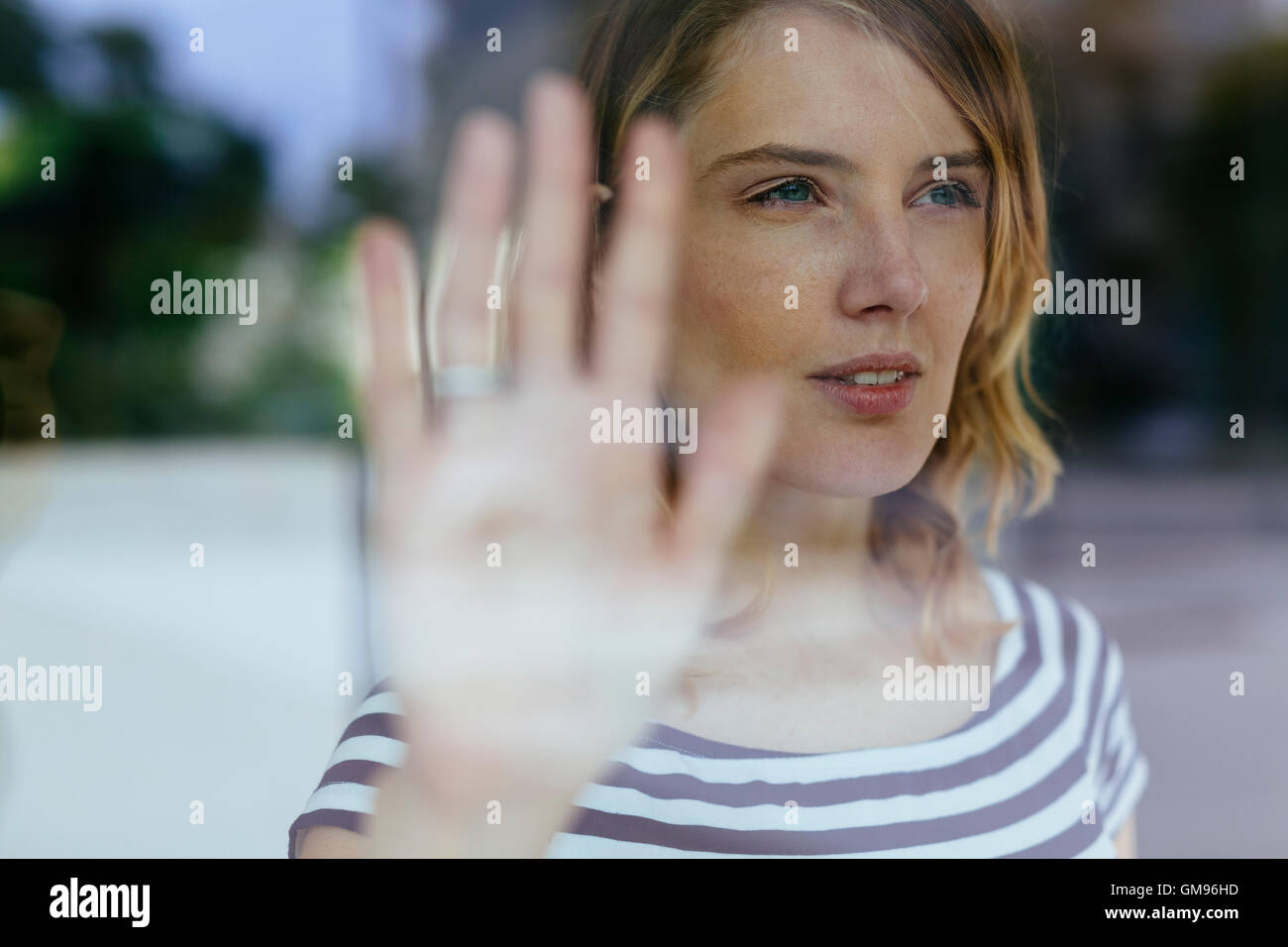 Portrait of young woman looking through window touching glass with her ...