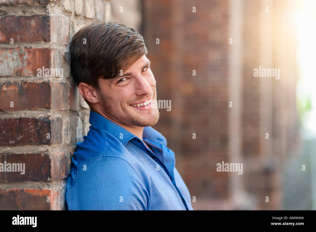 Smiling young man leaning against brick building Stock Photo - Alamy