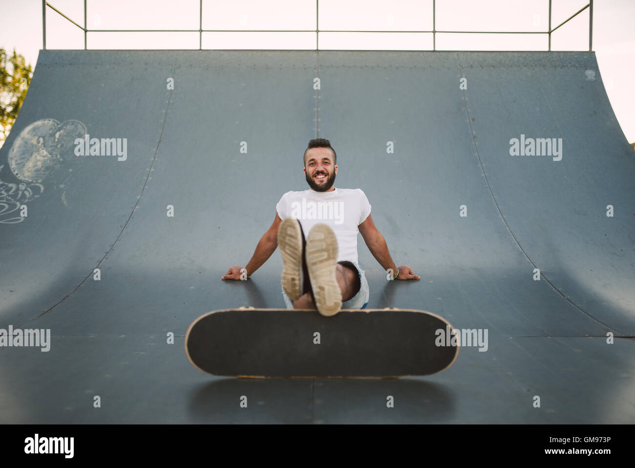 Smiling skateboarder sitting on ramp in a skatepark Stock Photo - Alamy