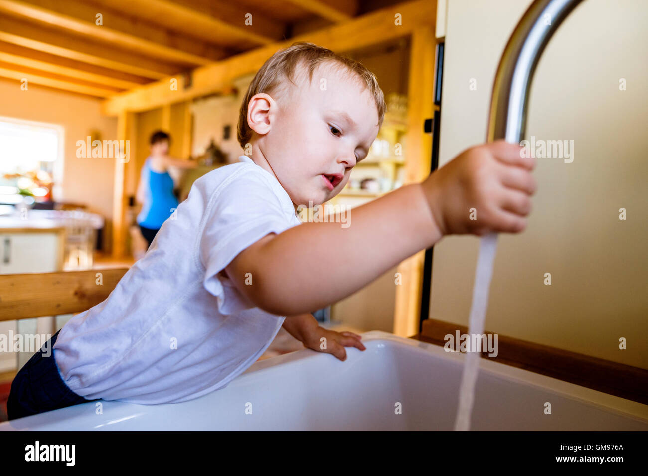 Little boy playing with tap in kitchen Stock Photo - Alamy