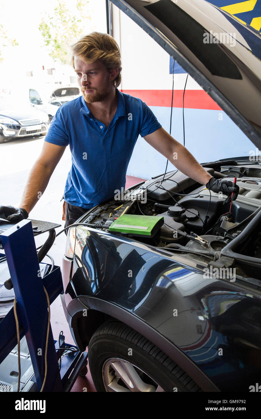 Mechanic fixing a car engine while using a computer in his workshop ...