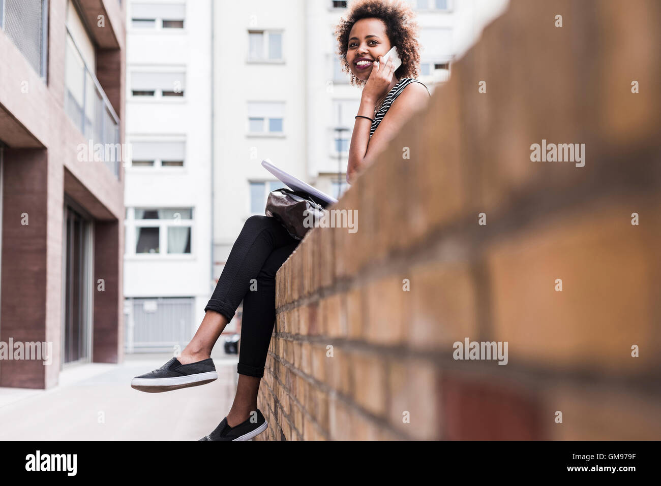 Young woman sitting on wall telephoning with cell phone Stock Photo - Alamy