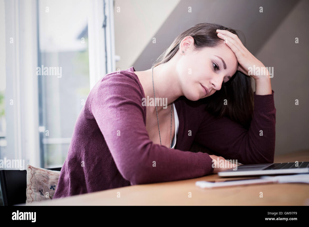 Young woman at desk resting her head in hand Stock Photo - Alamy