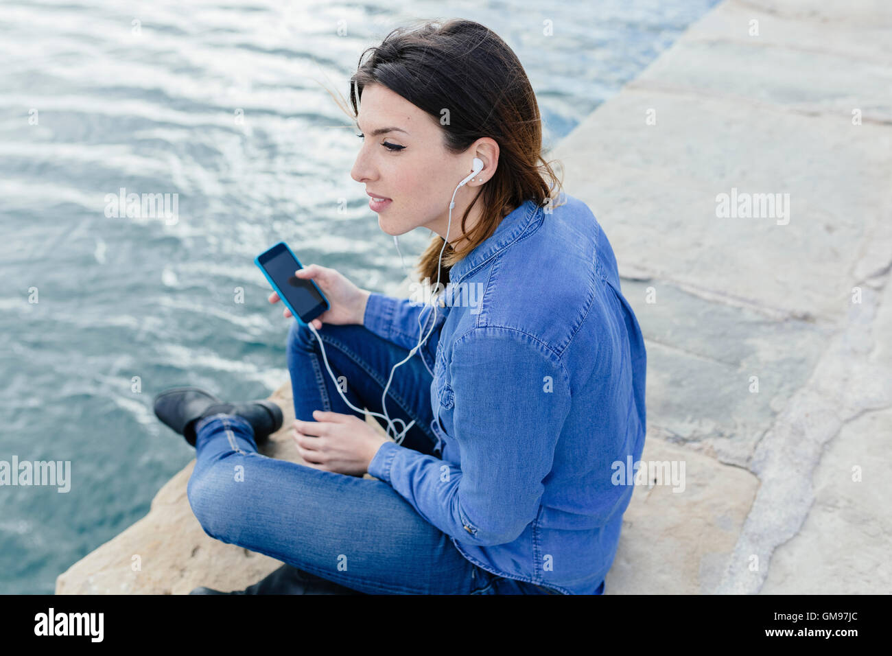 Young woman sitting on dock listening to music Stock Photo - Alamy