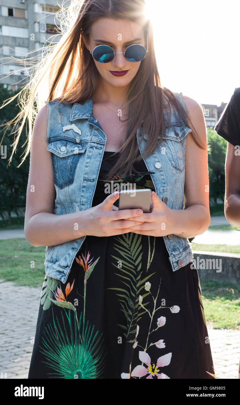 Woman with sunglasses standing at backlight looking at cell phone Stock ...