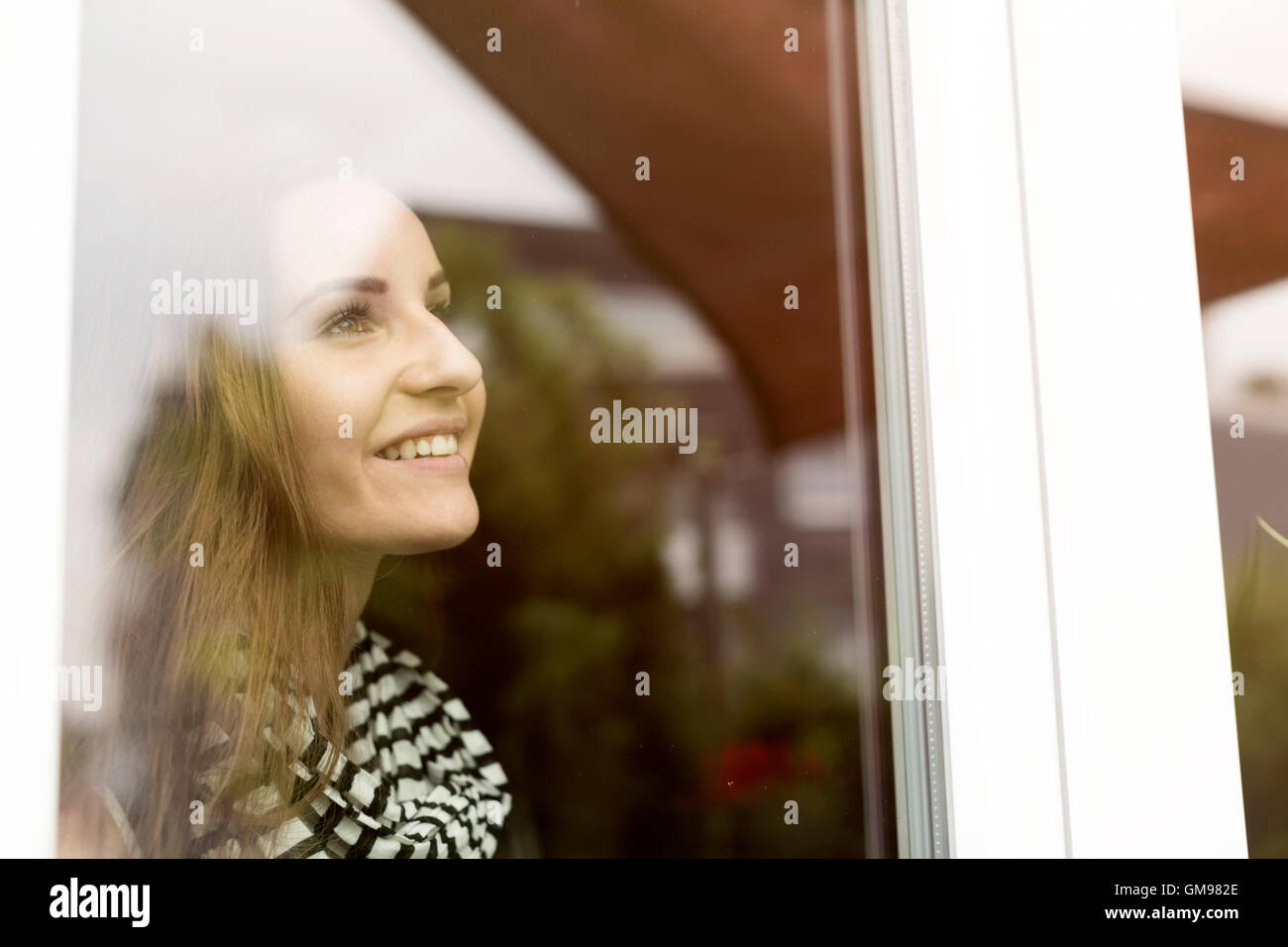 Young woman looking out of window, smiling Stock Photo - Alamy