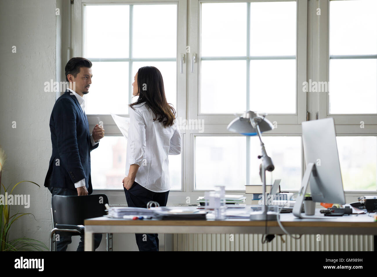 Businessman and woman standing at office window, disussing Stock Photo ...